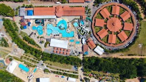 Vista aérea de um resort com várias piscinas, um edifício central amplo e uma estrutura circular com telhados vermelhos.