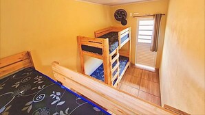 Um dormitório com beliches, ventilador de teto e janela com cortinas.