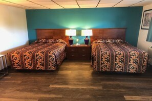 Quarto de hotel com duas camas, cabeceira de madeira, mesa de cabeceira com luminárias e uma parede cor de verde-água.