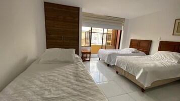 Quarto de hotel com duas camas de solteiro, guarda-roupa de madeira, uma mesinha e varanda com grade de metal.