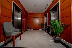 Um corredor com dois elevadores, uma cadeira cinzenta e um vaso de planta.