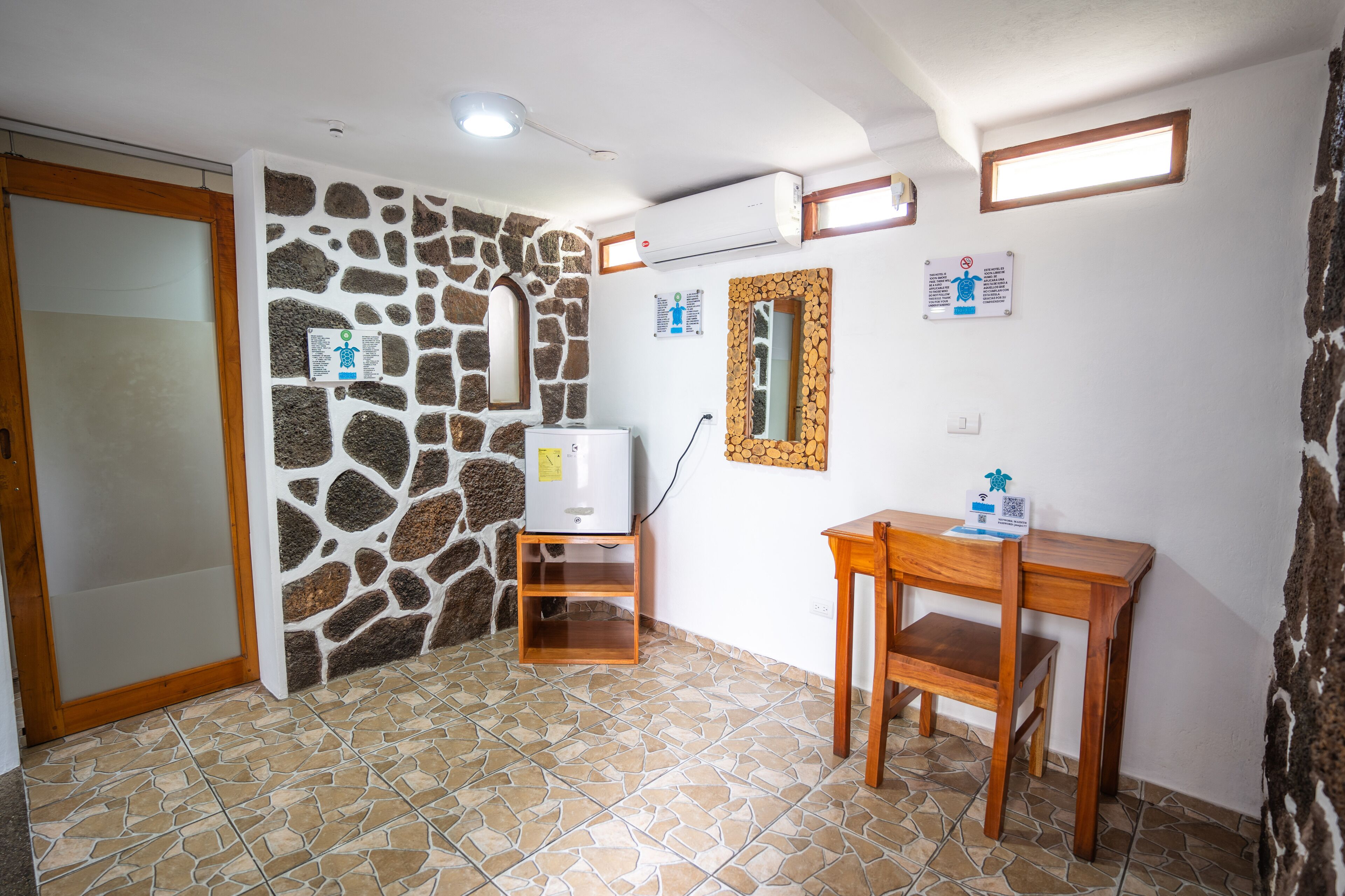 Quarto com parede de pedra, mesa de madeira, televisão e espelho.
