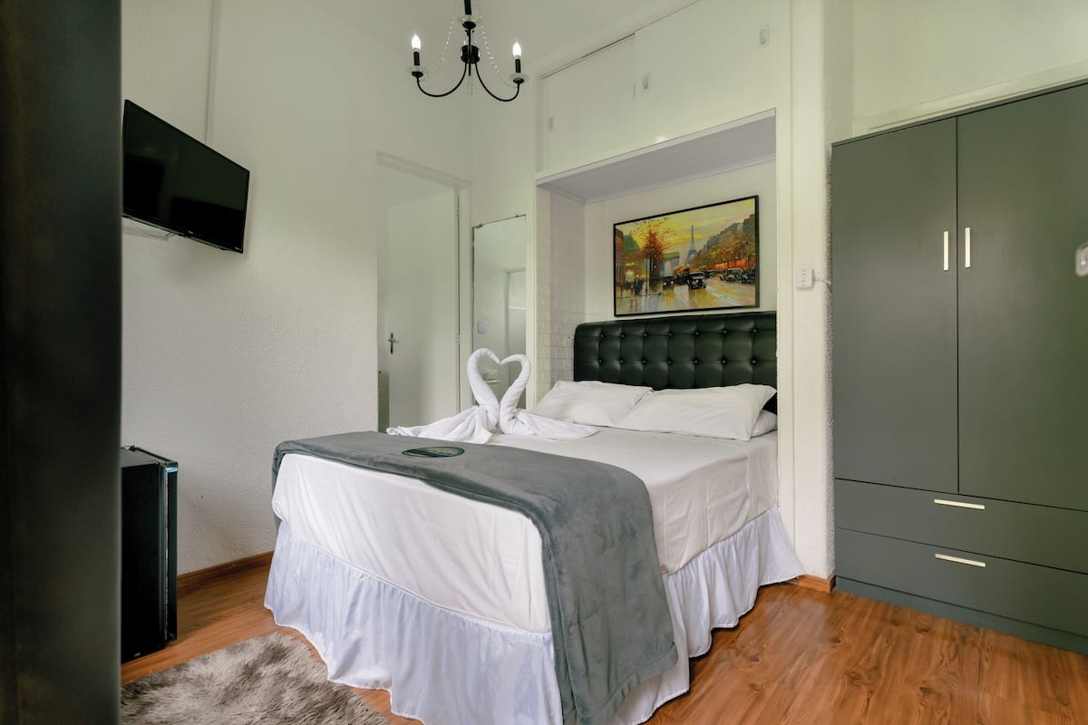 Quarto com cama, televisão, guarda-roupa e um quadro na parede.