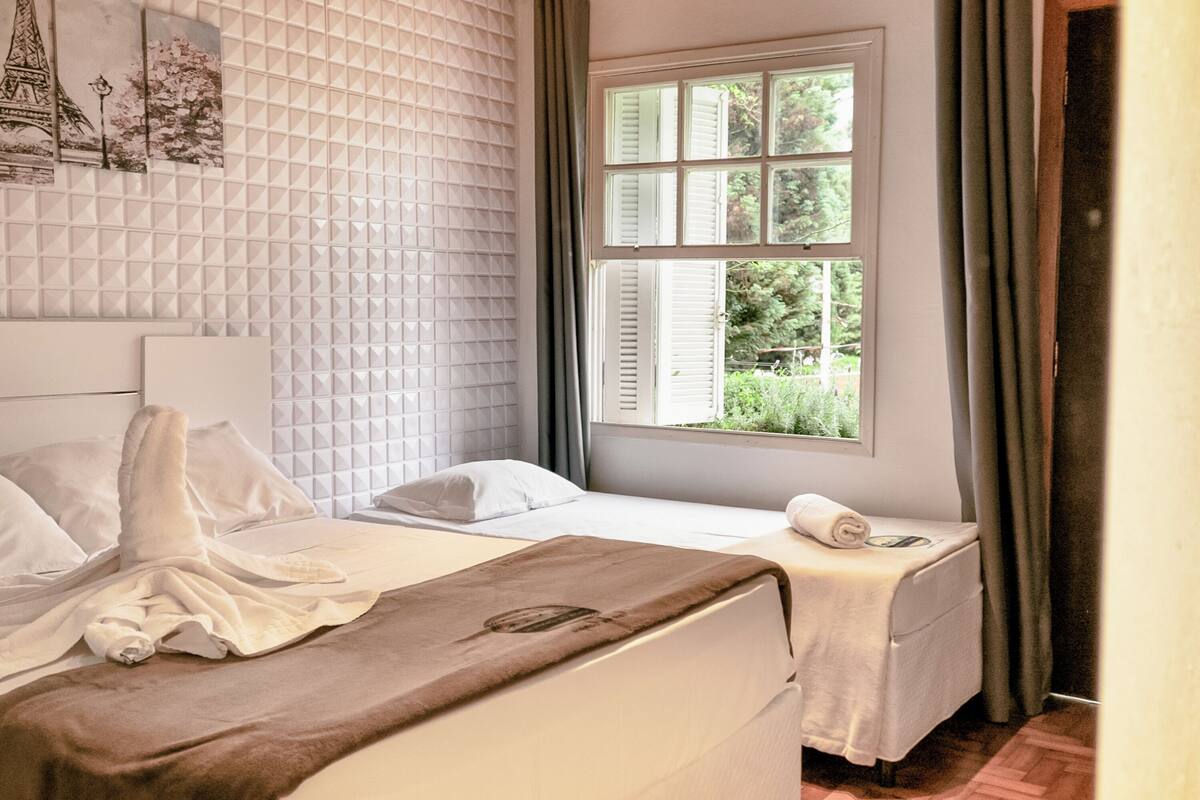 Quarto de hotel com uma cama, uma janela com cortinas e uma parede com padrão geométrico.