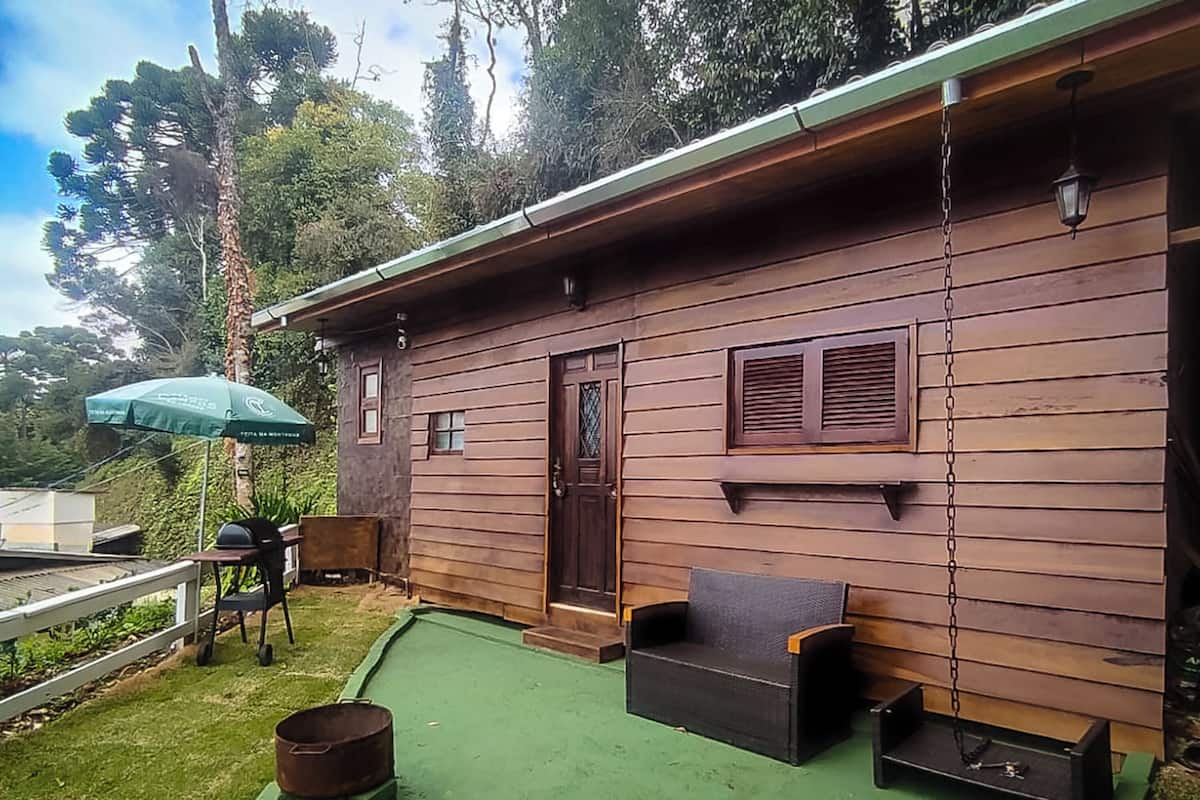Uma cabana de madeira com varanda, balanço e área de churrasco.