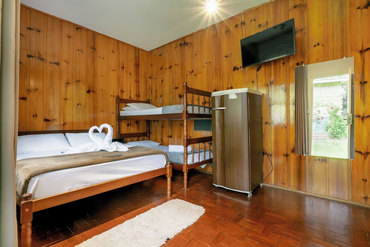 Quarto com paredes de madeira, uma cama beliche, um refrigerador e uma televisão.