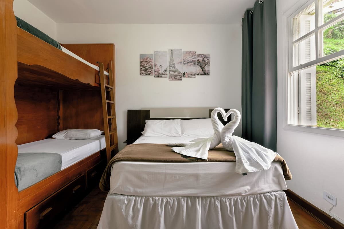 Um quarto com uma cama beliche, uma cama de solteiro, uma escada, uma obra de arte na parede e uma janela com cortinas.
