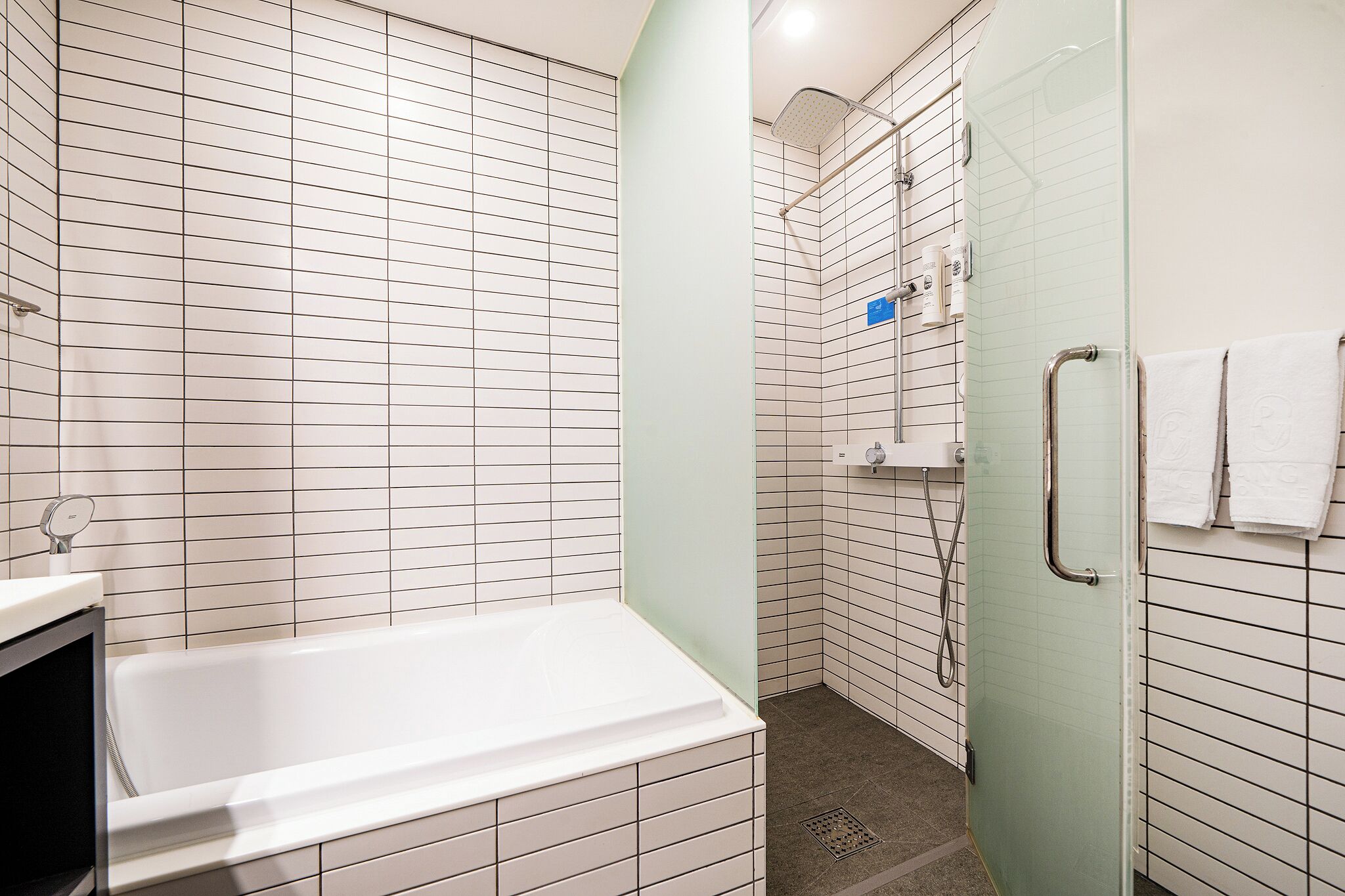 Um banheiro moderno com banheira branca, chuveiro com box de vidro e parede revestida com azulejos.