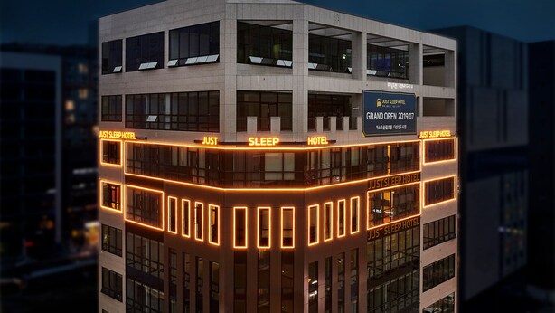 Um hotel moderno com placa indicando inauguração em 2019. Apresenta uma estrutura em vários andares, grandes janelas e fachada iluminada marcante.
