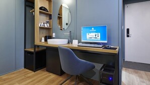 Quarto de hotel moderno com escrivaninha de madeira, um computador, uma cadeira, pia pequena e espelho.