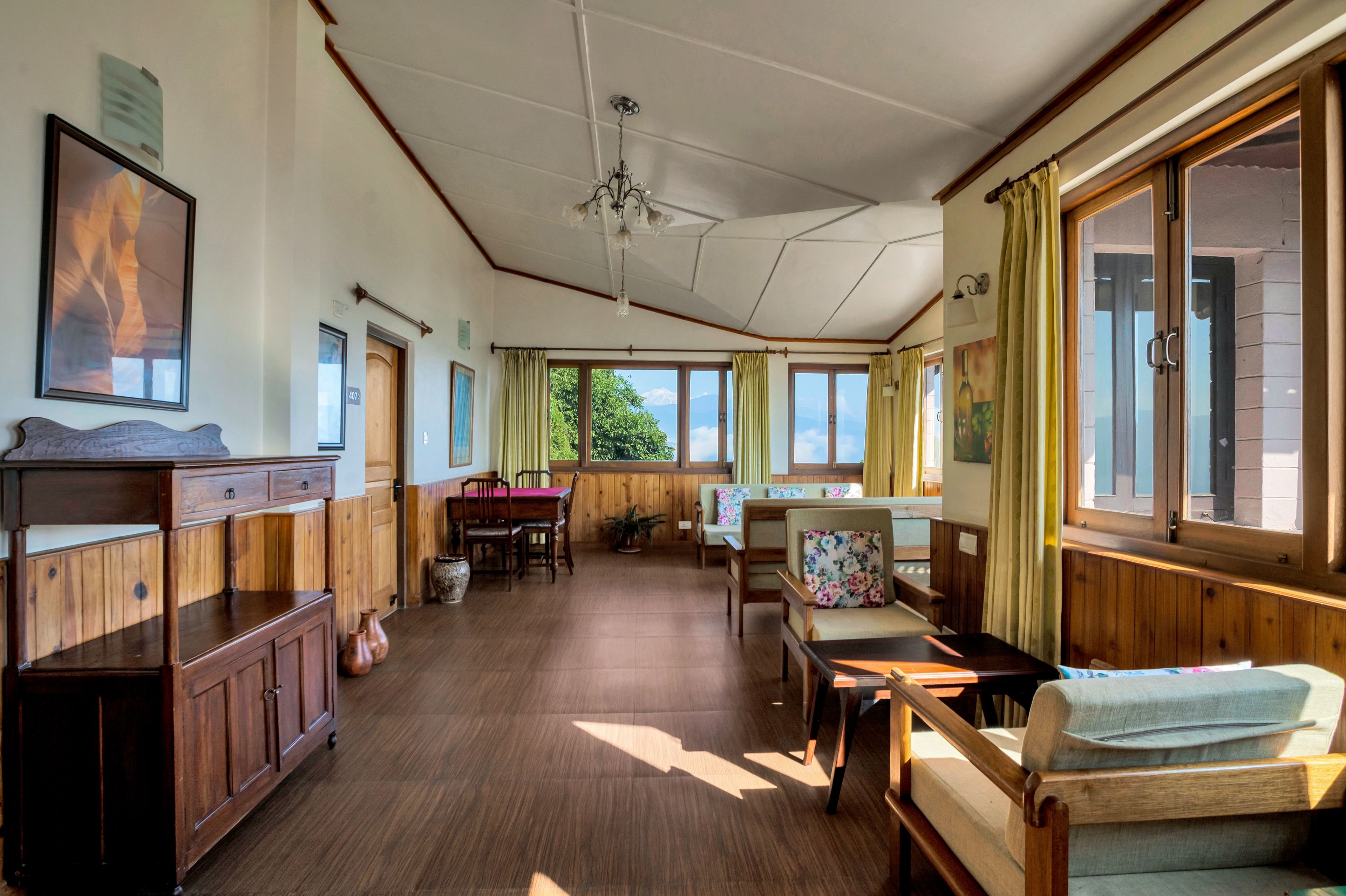 Um quarto espaçoso com painéis de madeira, área de jantar e grandes janelas com vista para o exterior.