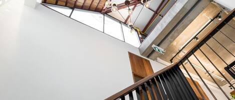 Um interior moderno com teto alto, vigas aparentes e escada com guarda-corpo preto e de madeira.