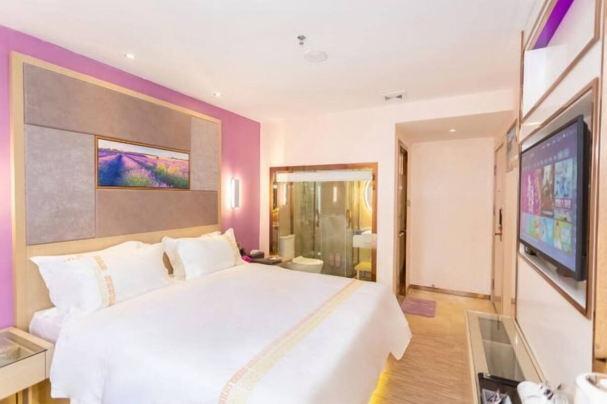 Quarto de hotel com uma cama grande, televisão, banheiro e divisória de vidro.