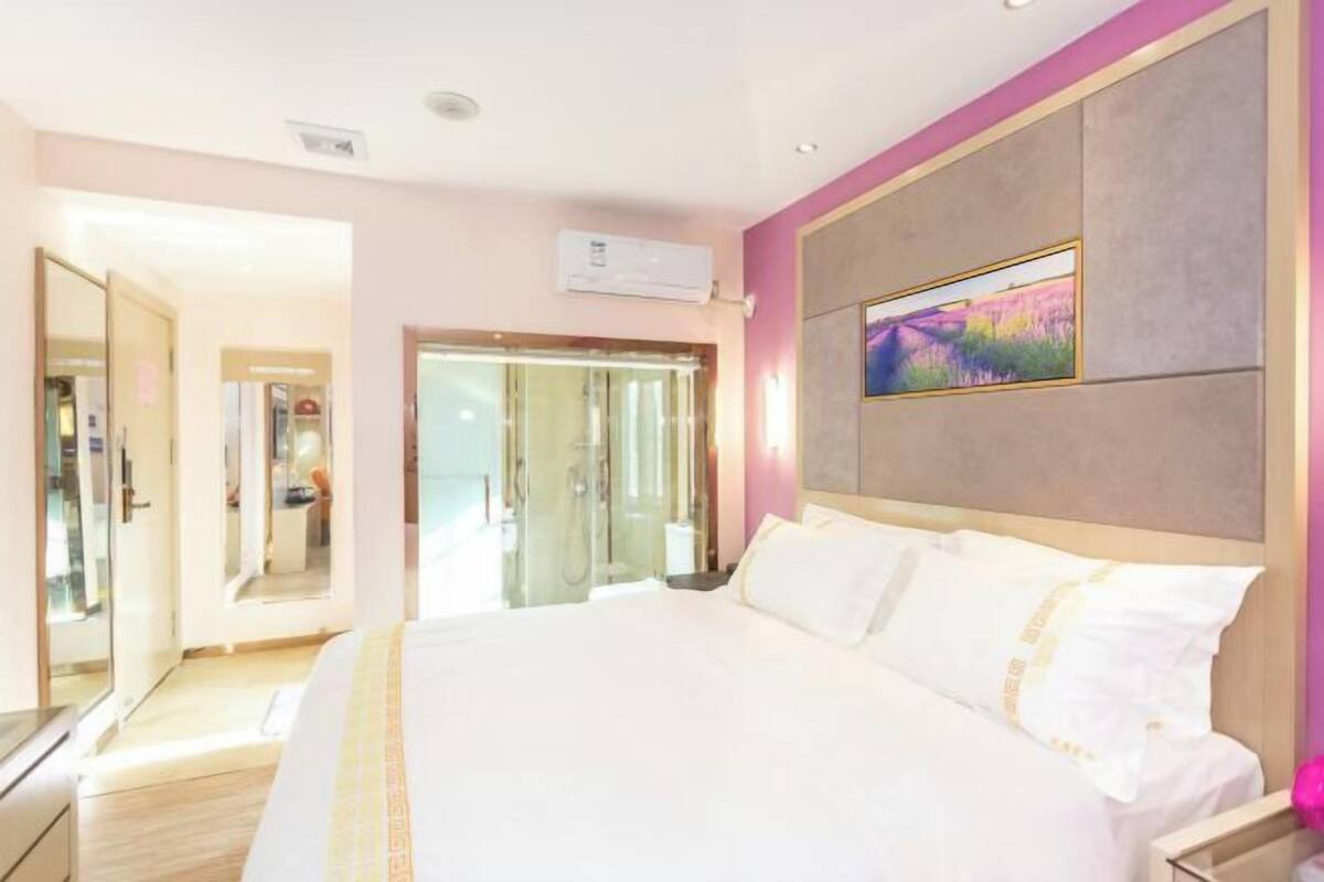 Quarto de hotel com cama, espelho, área de chuveiro e um quadro na parede.