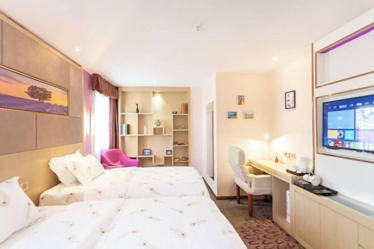 Quarto de hotel com cama, escrivaninha, cadeira, televisão e estante.