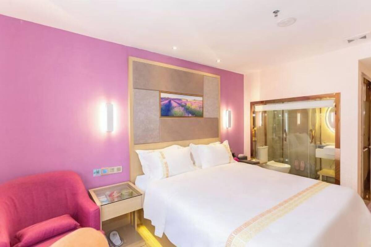 Quarto de hotel com uma cama grande, parede rosa e box de vidro.