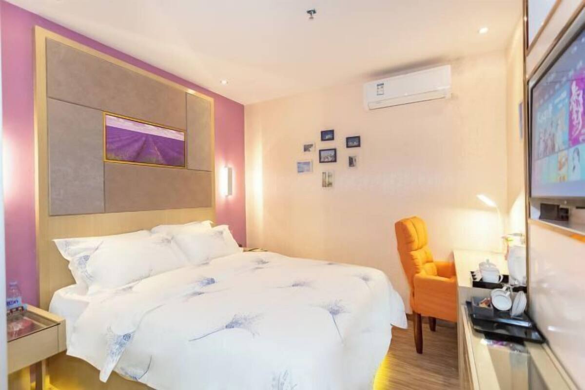 Quarto de hotel com cama, poltrona, escrivaninha e televisão na parede.