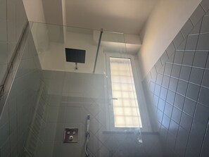 Área de chuveiro com porta de vidro, janela e painel de controle.