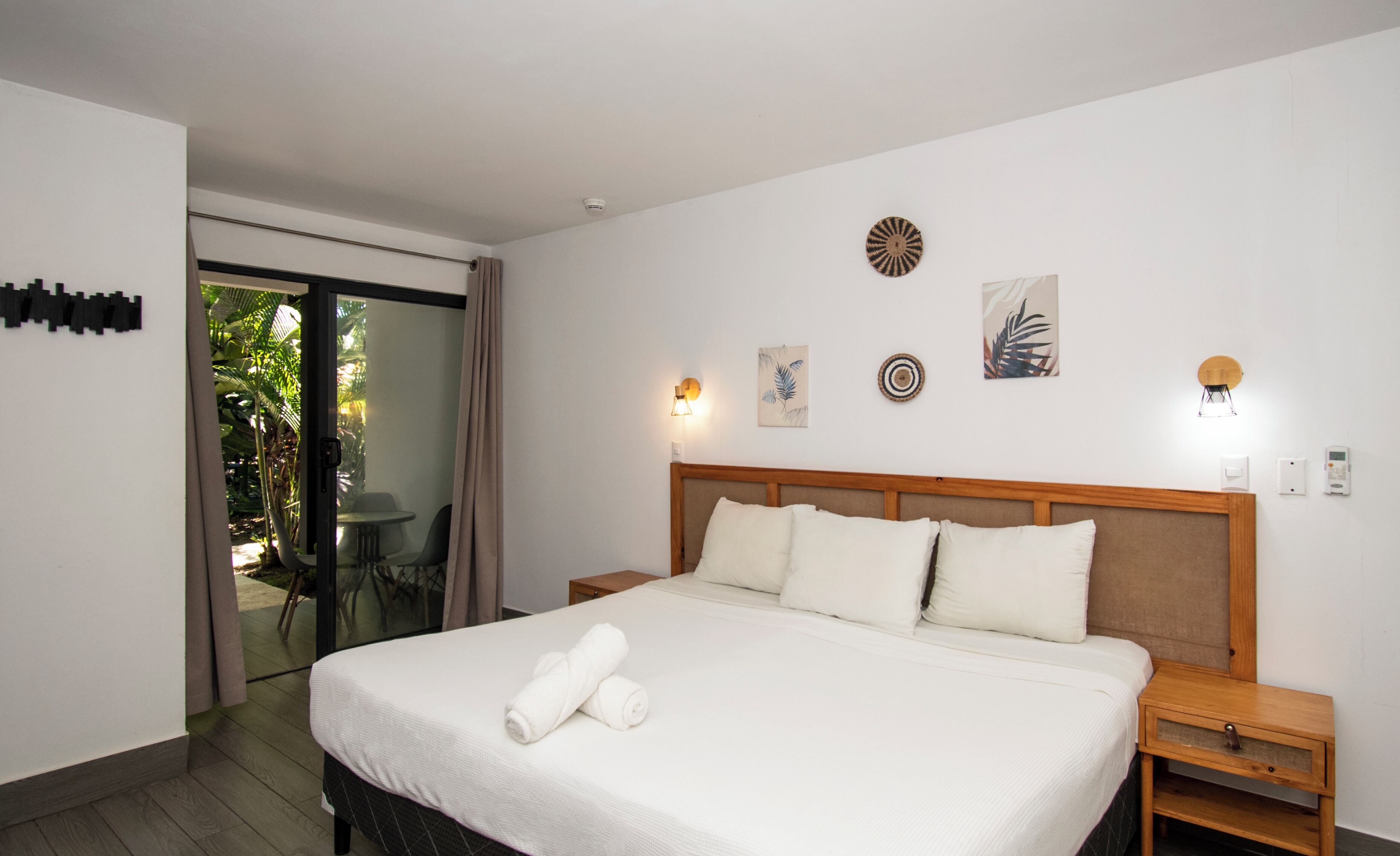 Quarto de hotel com cama, mesa de cabeceira, luminária na parede e vista para o exterior.