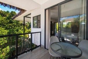 Varanda com porta de vidro, mesa redonda e cadeiras, com vista para um jardim exuberante.