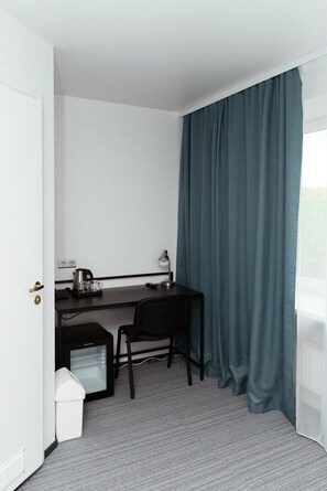 Quarto pequeno com escrivaninha, cadeira e frigobar.