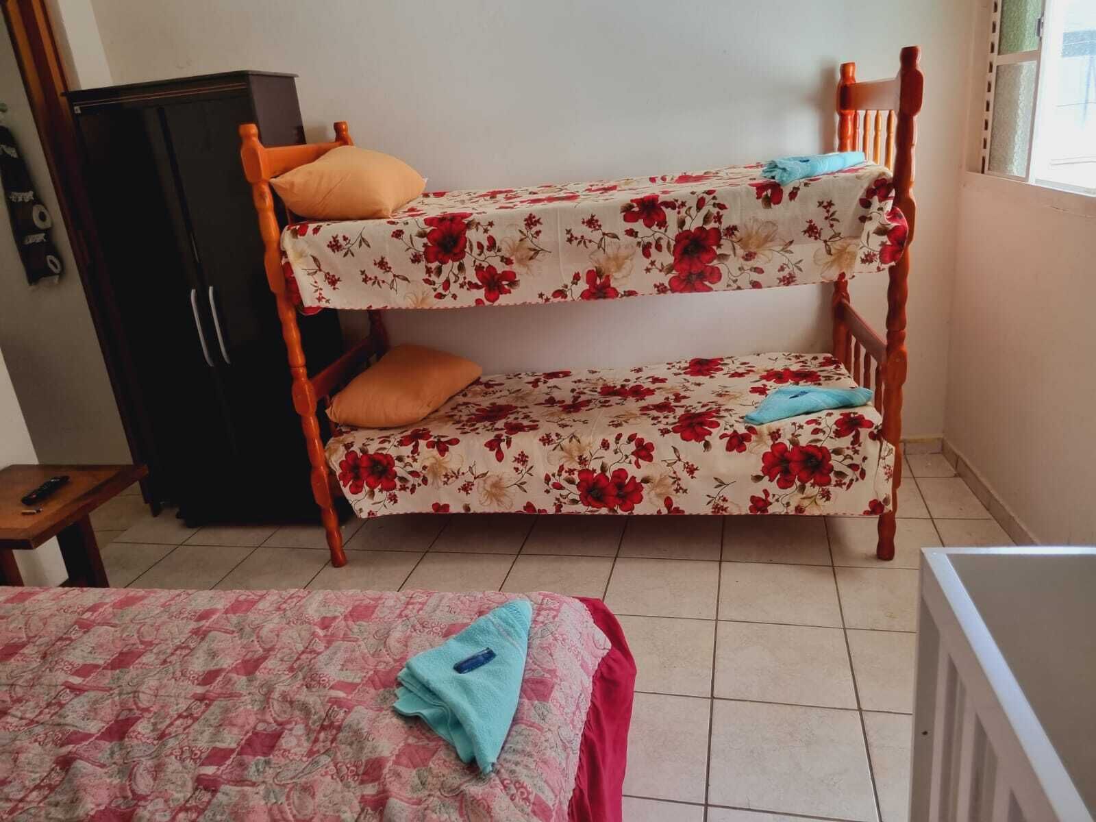 Uma cama beliche com roupa de cama floral, uma mesinha e um guarda-roupa em um quarto com piso de azulejos.