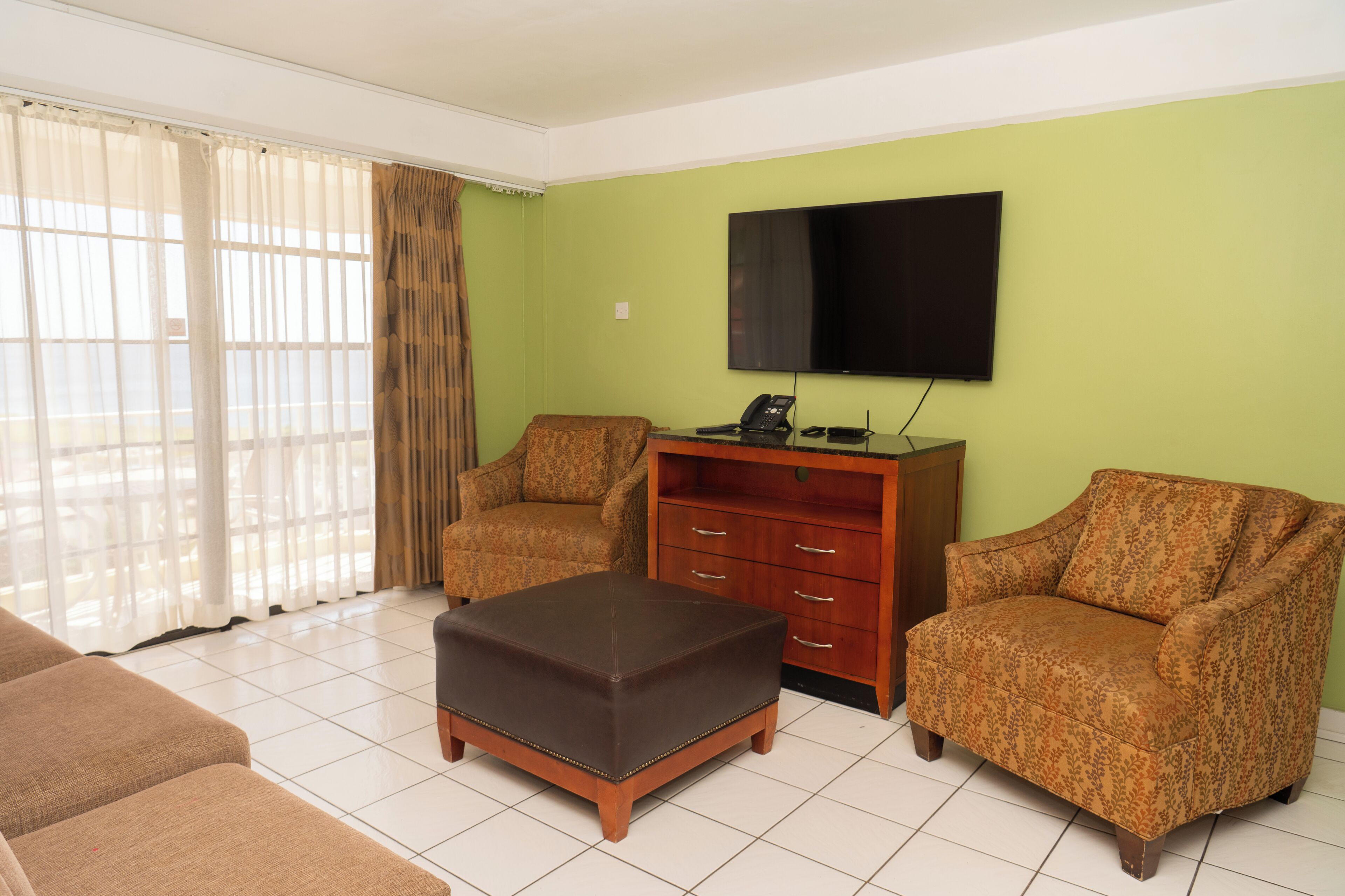 Sala de estar com sofá, duas poltronas, mesa de centro, televisão e telefone sobre um aparador de madeira.