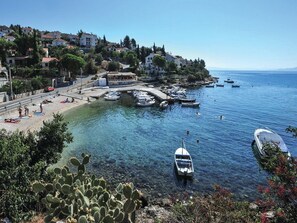 Uma cidade costeira com um porto tranquilo, barcos atracados e uma praia com pessoas.