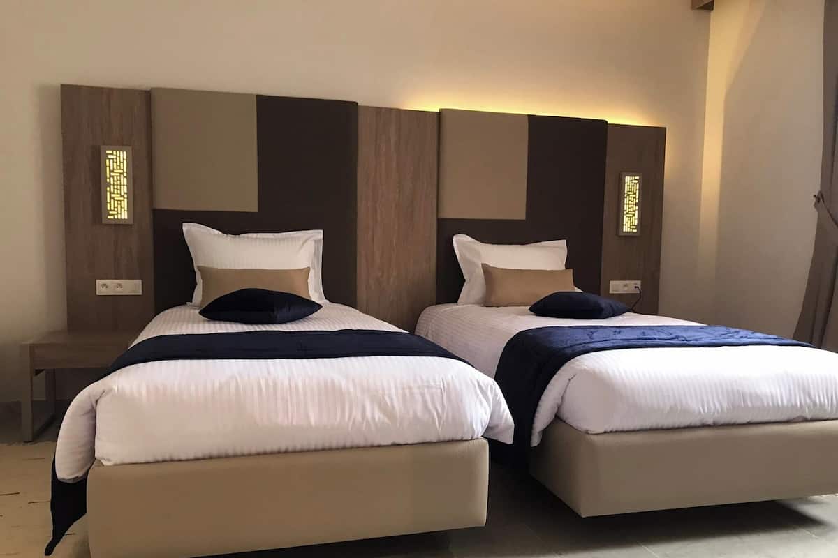 Quarto de hotel com duas camas, uma mesa de cabeceira e um aplique na parede.
