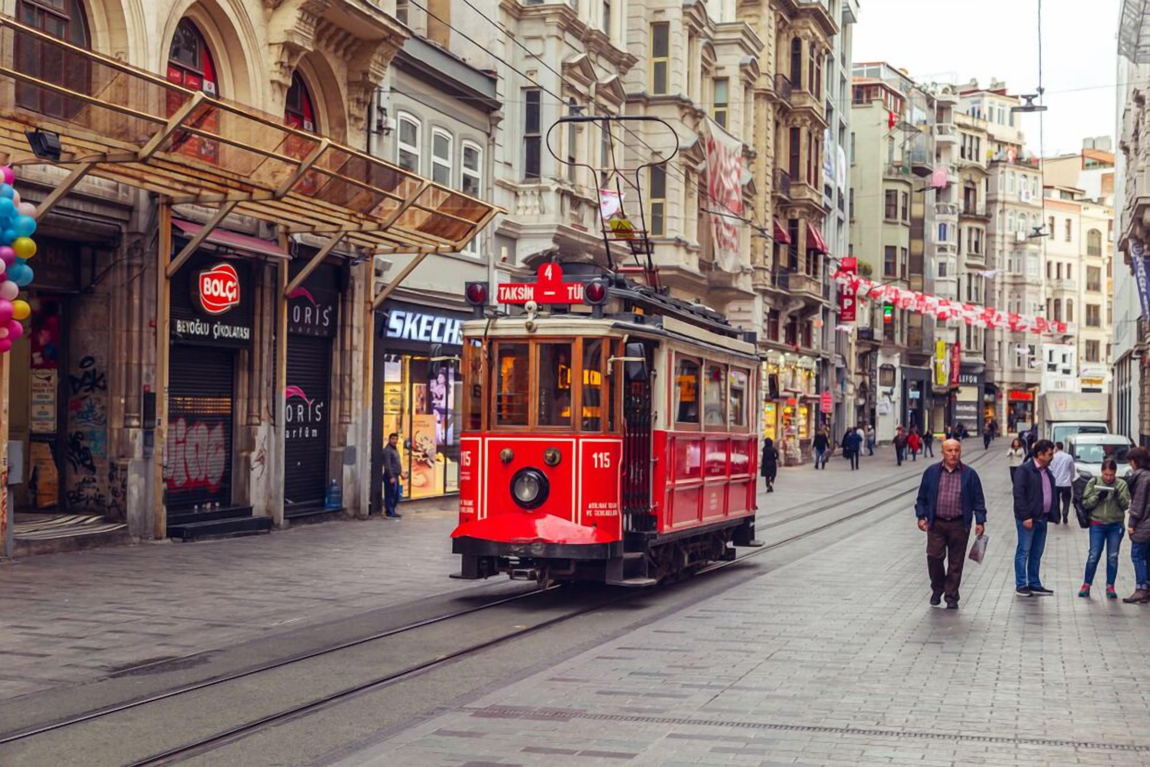 Um elétrico vermelho numa rua da cidade com lojas e pedestres.