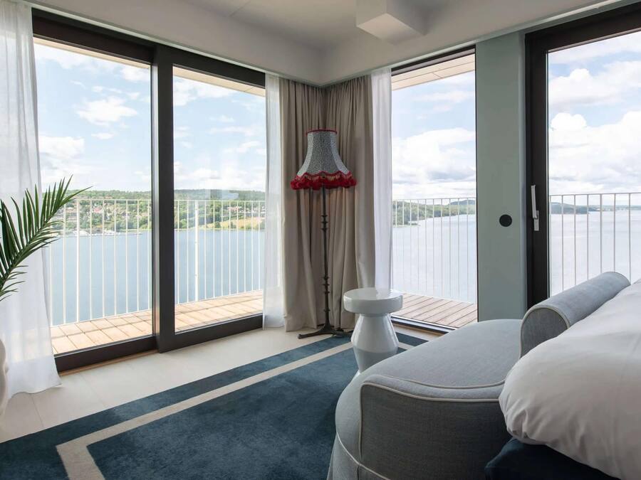 Quarto de hotel com uma cama grande, uma mesa de cabeceira, um abajur e vista para uma varanda com grade.