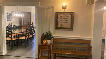 Uma sala de jantar com mesa e cadeiras, um banco, uma placa emoldurada e um vaso com planta.