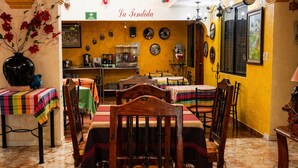 Interior de restaurante com mesas, cadeiras, área de cozinha e um relógio na parede.
