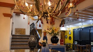 Um hall com um candelabro, uma estátua, um vaso com flores e uma escadaria.
