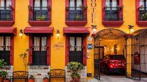 Um hotel com fachada amarela, detalhes em vermelho e várias varandas com plantas em vasos.