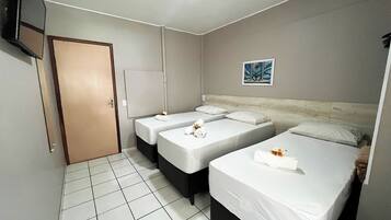 Quarto de hotel com duas camas de solteiro, cabeceira de madeira, televisão de tela plana na parede e piso revestido de azulejos.