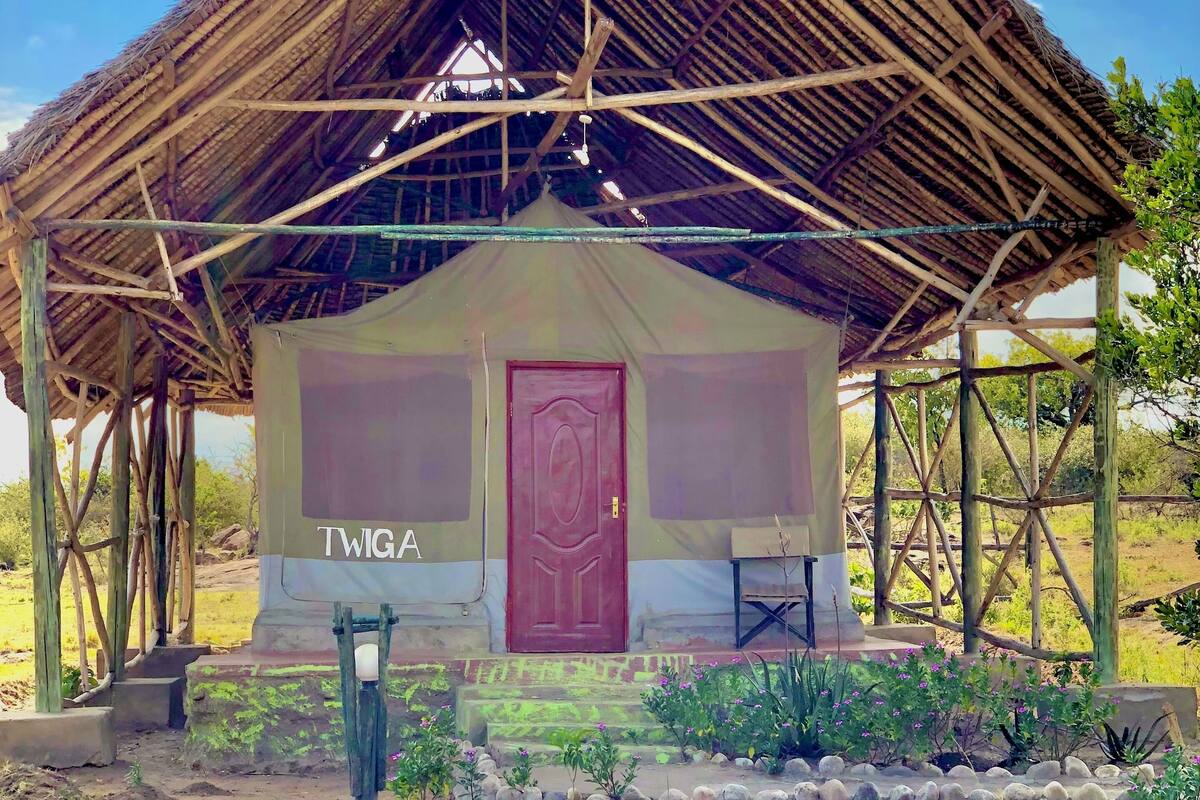 Uma construção com telhado de palha e uma porta vermelha, com a placa 