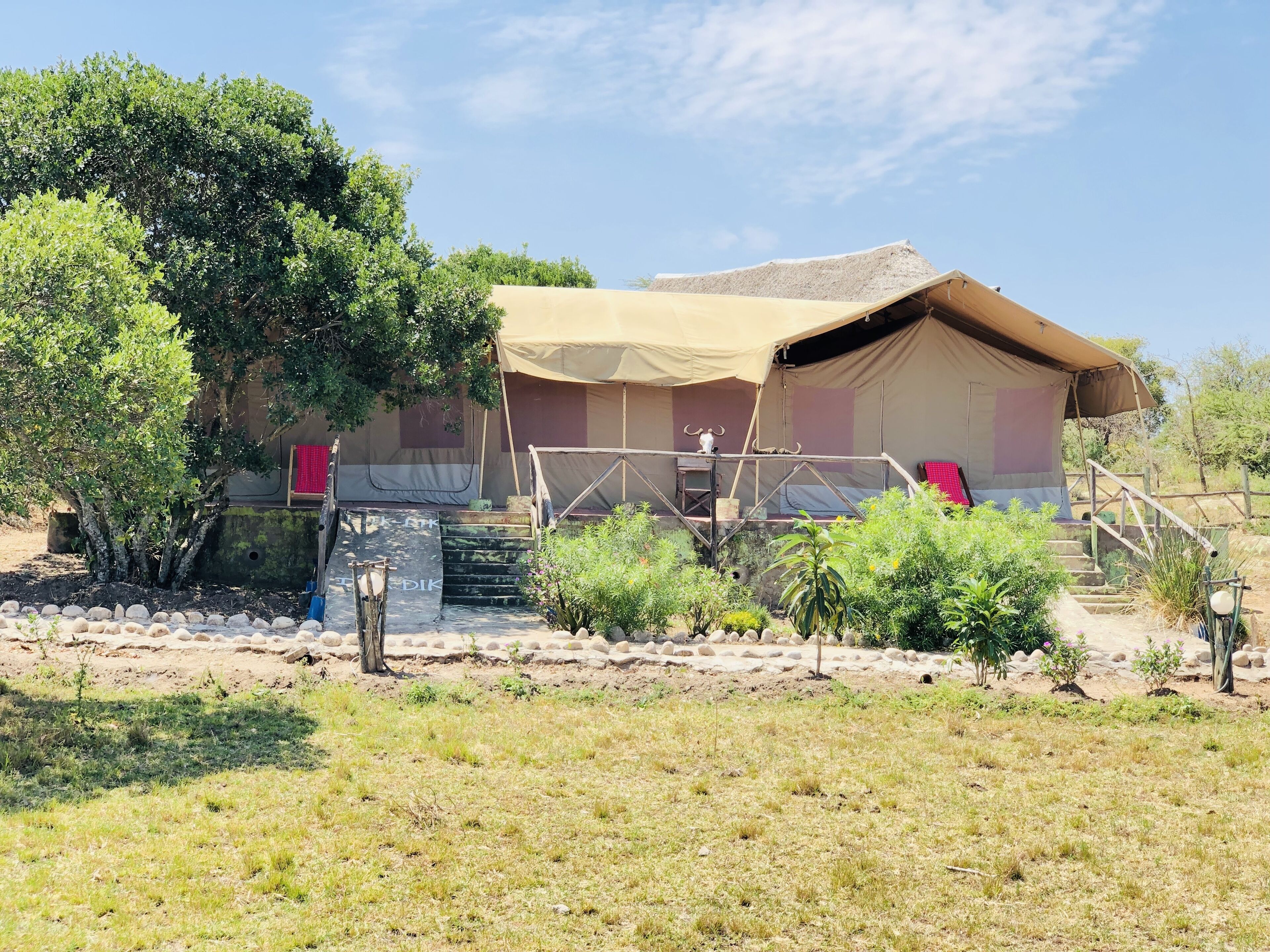 Uma pousada de safari com uma grande estrutura de tenda, uma escadaria que leva à entrada e uma paisagem ao redor com vegetação escassa.