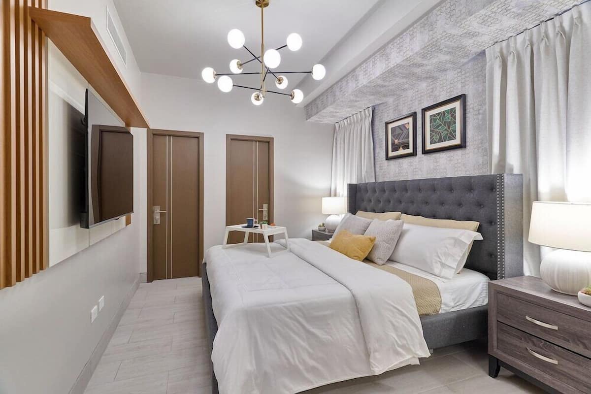 Quarto moderno com uma cama grande, mesas de cabeceira, televisão e um lustre.