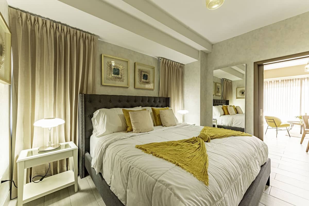 Quarto de hotel moderno com uma cama grande, mesas de cabeceira, um espelho e vista para a varanda.