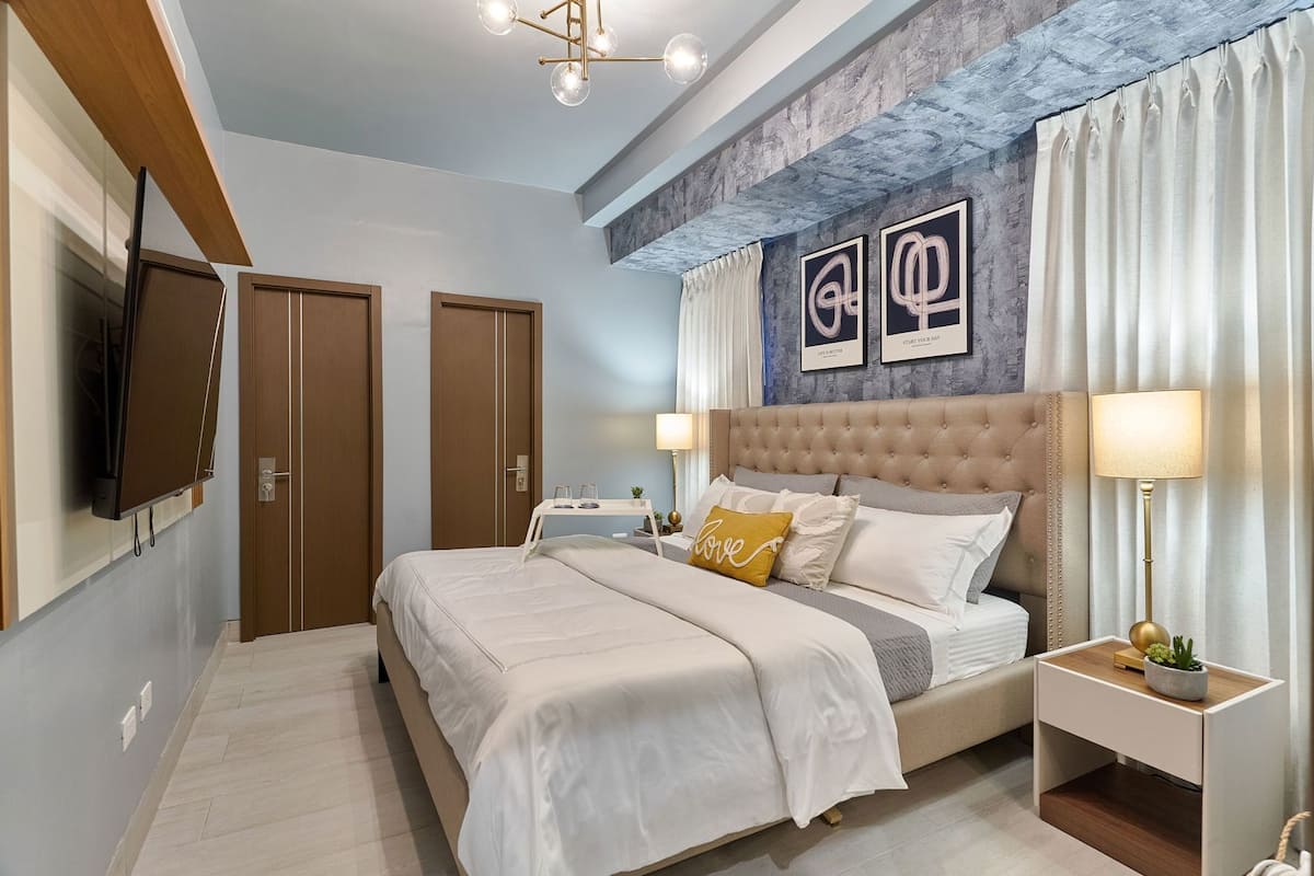 Quarto moderno com uma cama grande, mesas de cabeceira, televisão e obras de arte na parede.