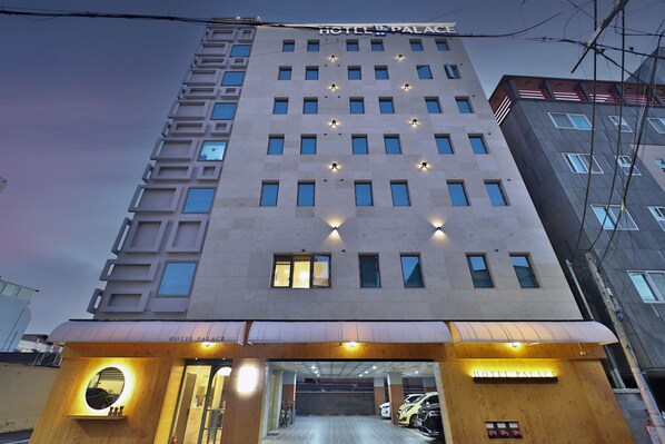 Um hotel de vários andares com fachada moderna, janelas iluminadas e entrada destacada com toldo.