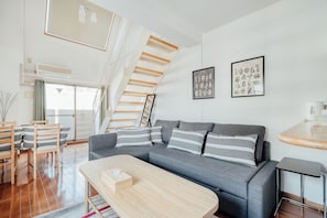 Uma sala de estar moderna com um sofá cinza, almofadas listradas, uma mesa de centro de madeira e uma escada com vigas de madeira.