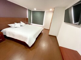 Quarto de hotel moderno com uma cama grande, cabeceira de madeira, mesa de cabeceira e uma janela ampla com vista.