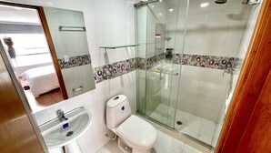 Casa de banho com cabine de chuveiro em vidro, sanita branca e lavatório.