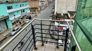 Vista de uma varanda com vista para uma rua, com edifícios, incluindo um prédio azul-turquesa e uma estrutura de vidro grande.