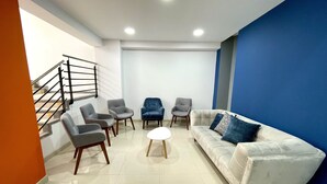Uma área de espera moderna com um sofá branco, várias poltronas, uma mesa de centro e uma escada com corrimão.