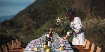 Uma mesa posta ao ar livre com garrafas de vinho, copos e flores.