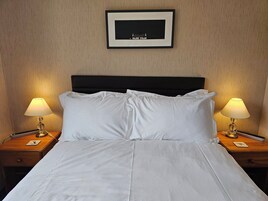 Uma cama bem arrumada com lençóis brancos, duas luminárias de cabeceira e um quadro na parede.