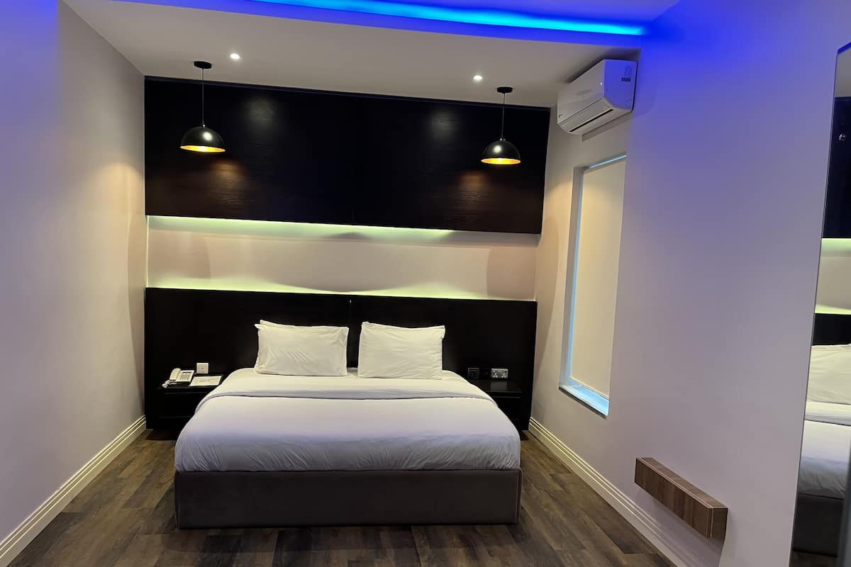 Quarto de hotel moderno com uma cama grande, duas mesas de cabeceira e uma janela.